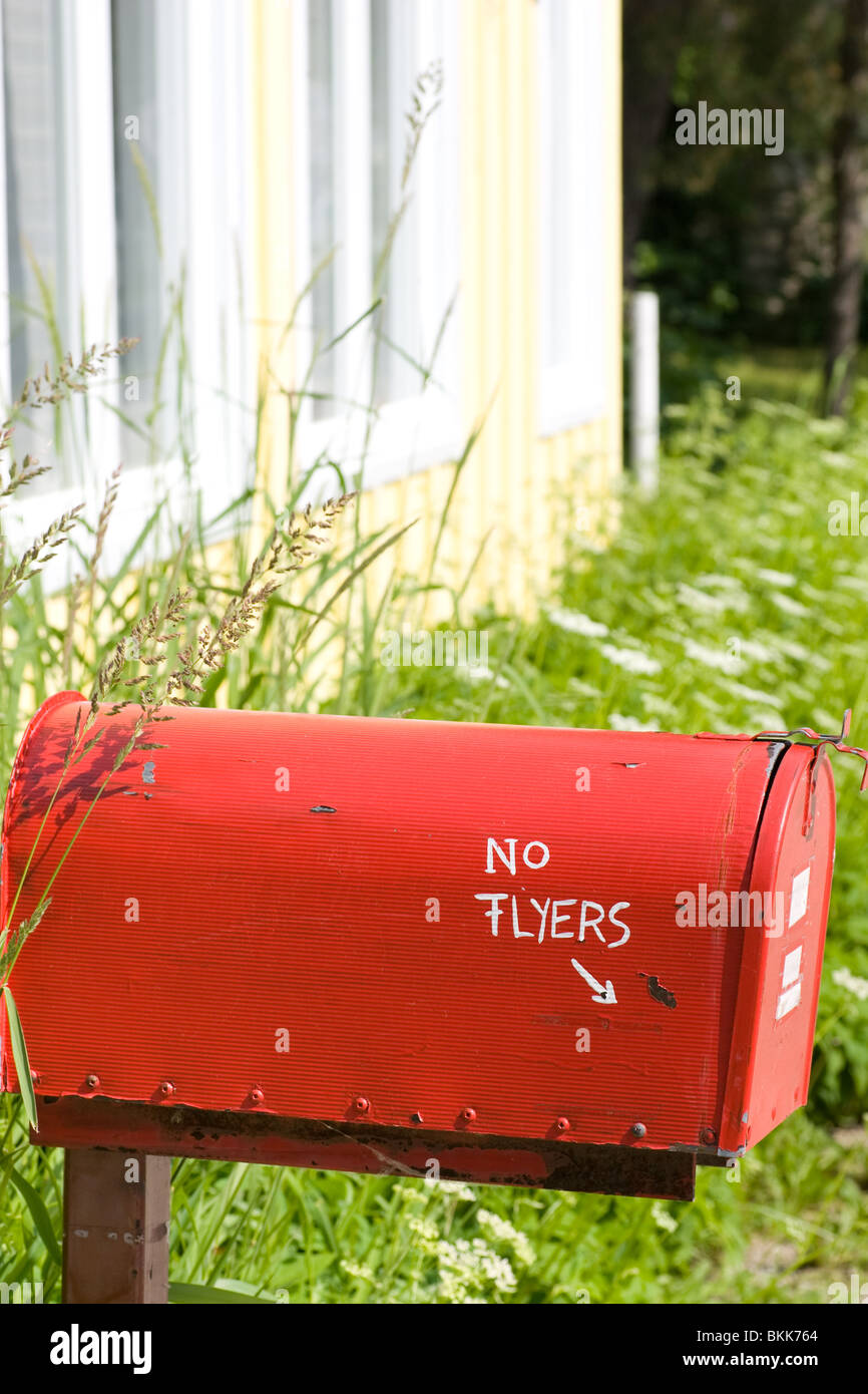 A bright red mailbox, surrounded by tall grass, with the corner of a ...