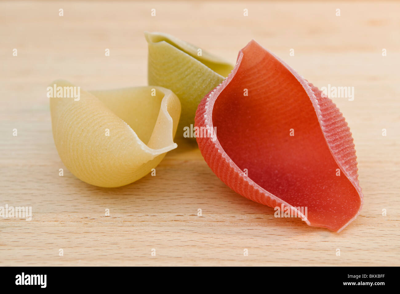 Large dried coloured pasta shells on pale wooden chopping board Stock ...