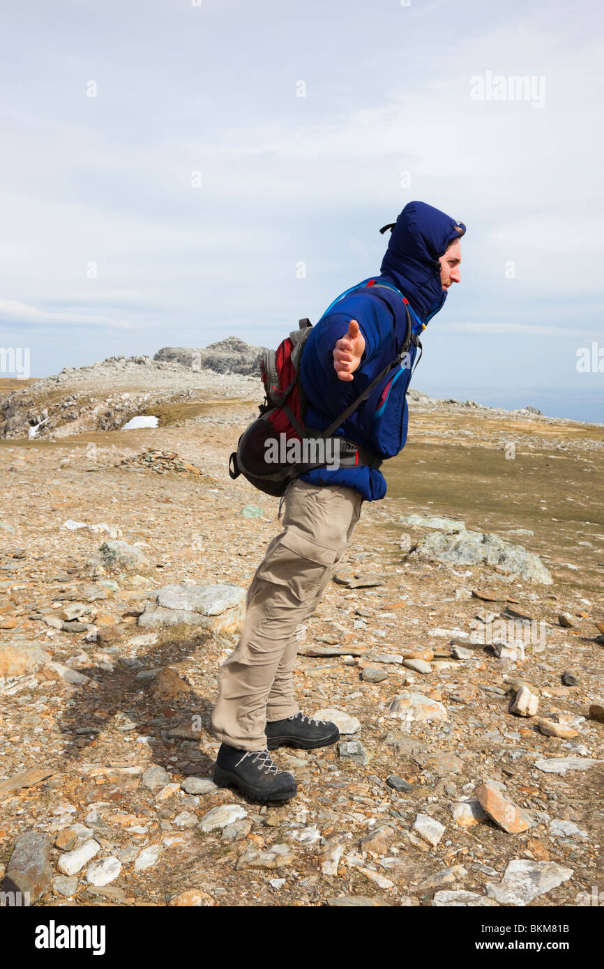 Man leaning in to the wind on a very windy day on exposed mountain top ...