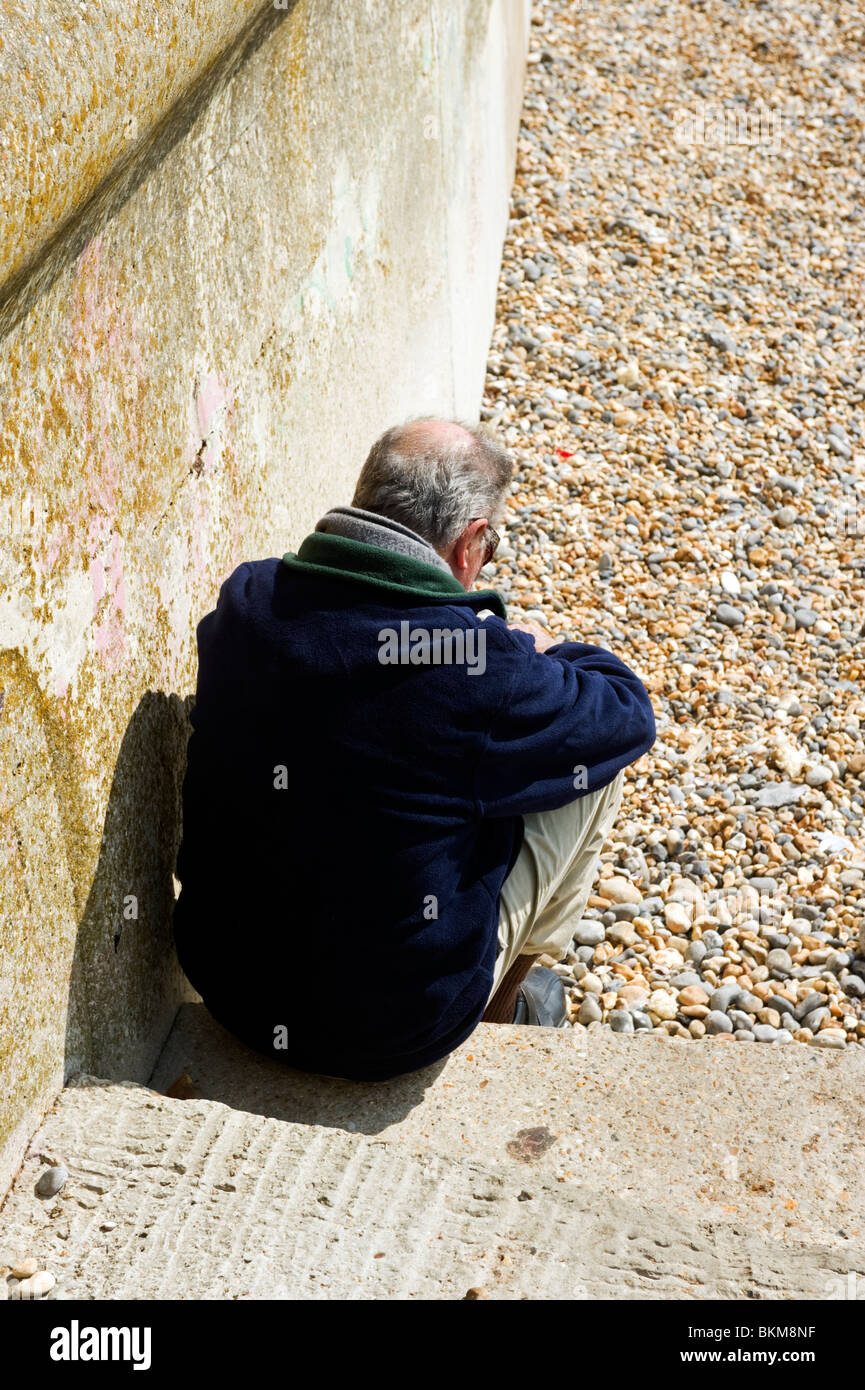 A middle aged man sitting hunched on concrete steps to Brighton shingle ...