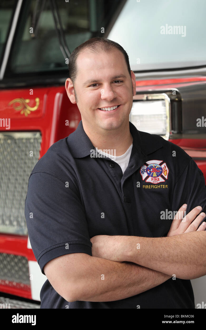 handsome fireman in his twenties with arms crossed standing in front of ...