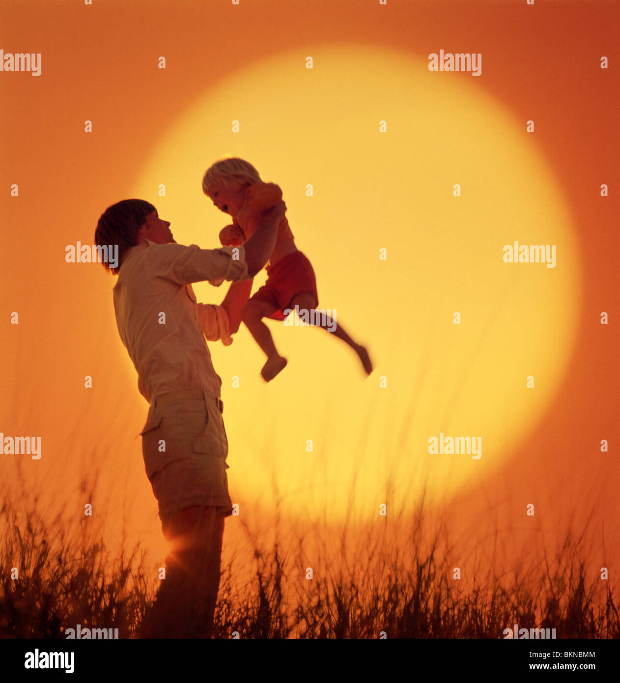 Father holding son with the sun setting in the background Stock Photo ...