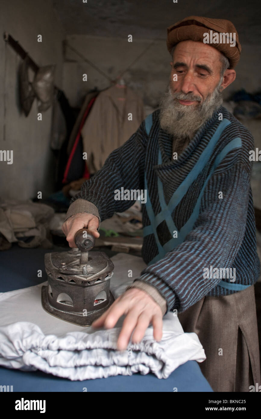 Old tailor ironing using a traditional coal iron in the Chitral region ...