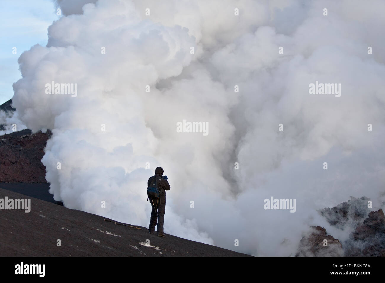 Tourist photographing steam clouds where lava flows meet snow and ice ...
