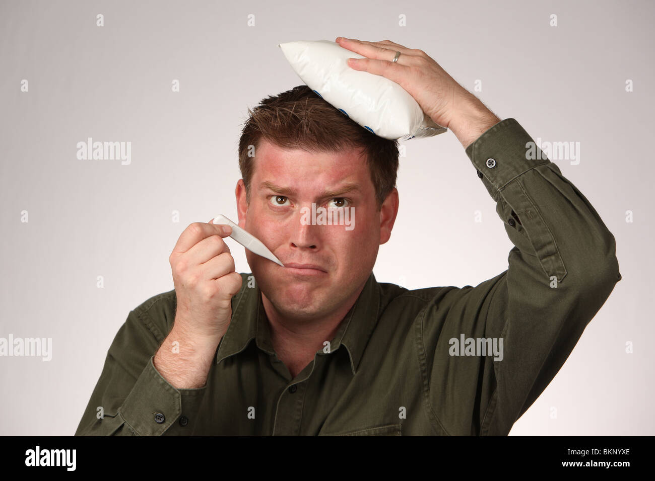 Sick man with digital thermometer in his mouth and ice pack on his head ...