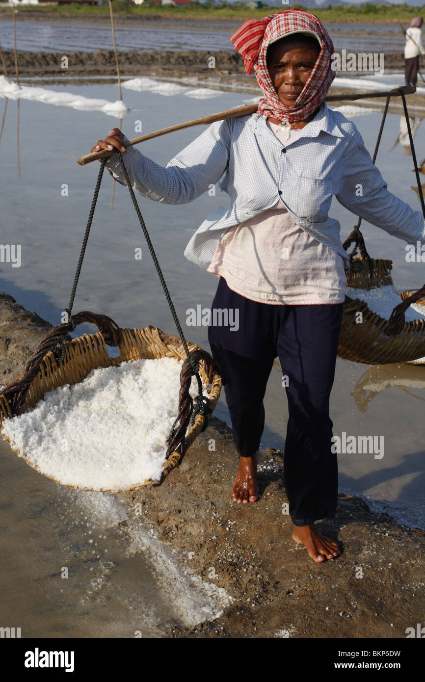 A woman carries a heavy load of salt on a salt farm near Kampot ...