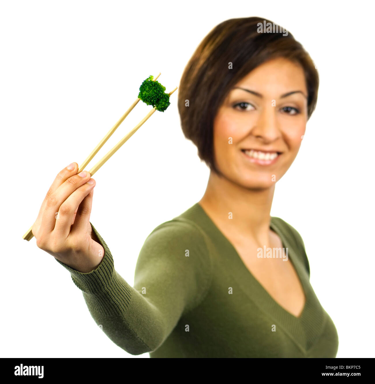 Smiling lady holds a green piece of cooked broccoli with chopsticks ...