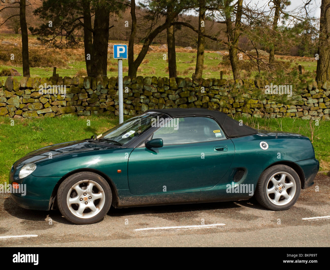 Green MG sports car parked on a bay in the countryside with stone wall ...