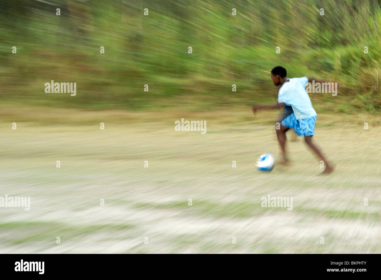 African child playing soccer barefoot in a field in Hout Bay in Cape ...