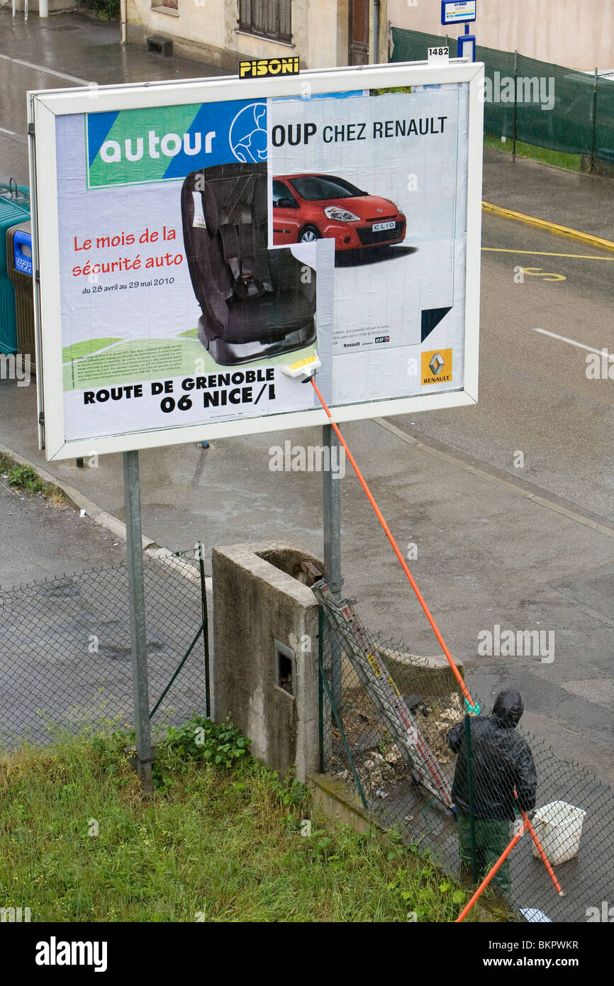 Man posting an advert to a billboard beside a road using a ladder and ...