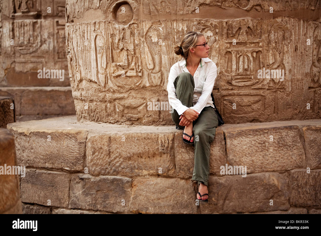 Egypt, Karnak. A tourist sits at the base of a massive stone column in ...