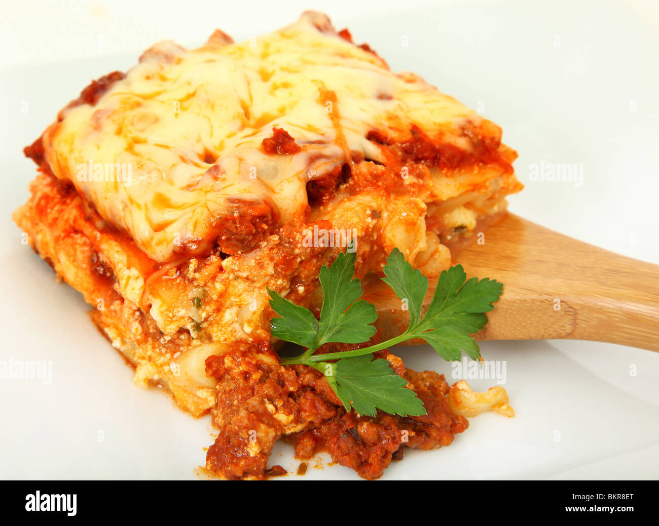 Square of baked lasagna with parsley on bamboo serving spoon Stock ...