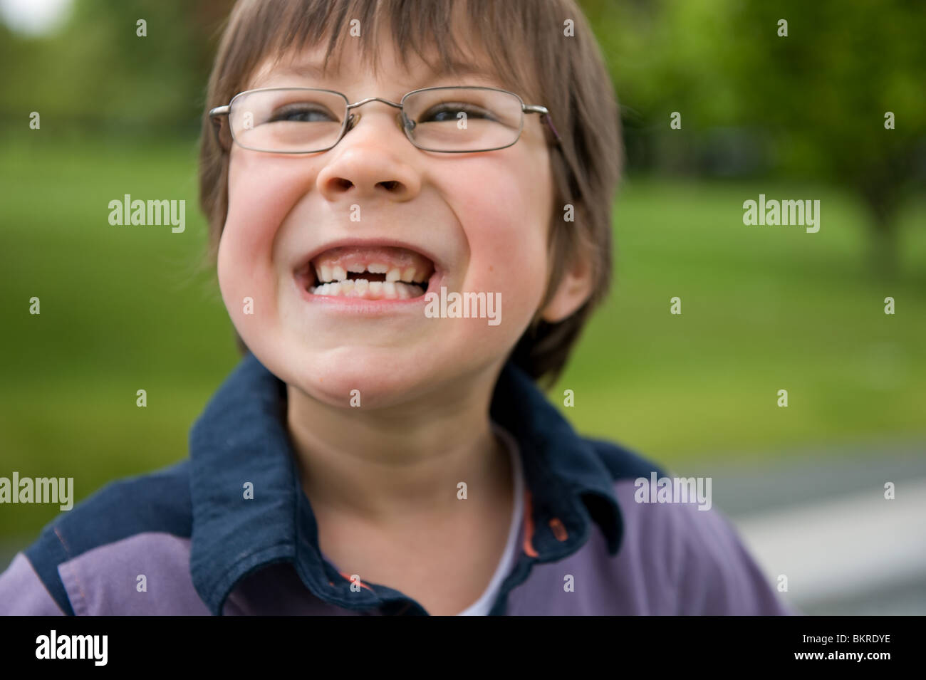 A young boy of seven years with missing front teeth, outside in a park ...