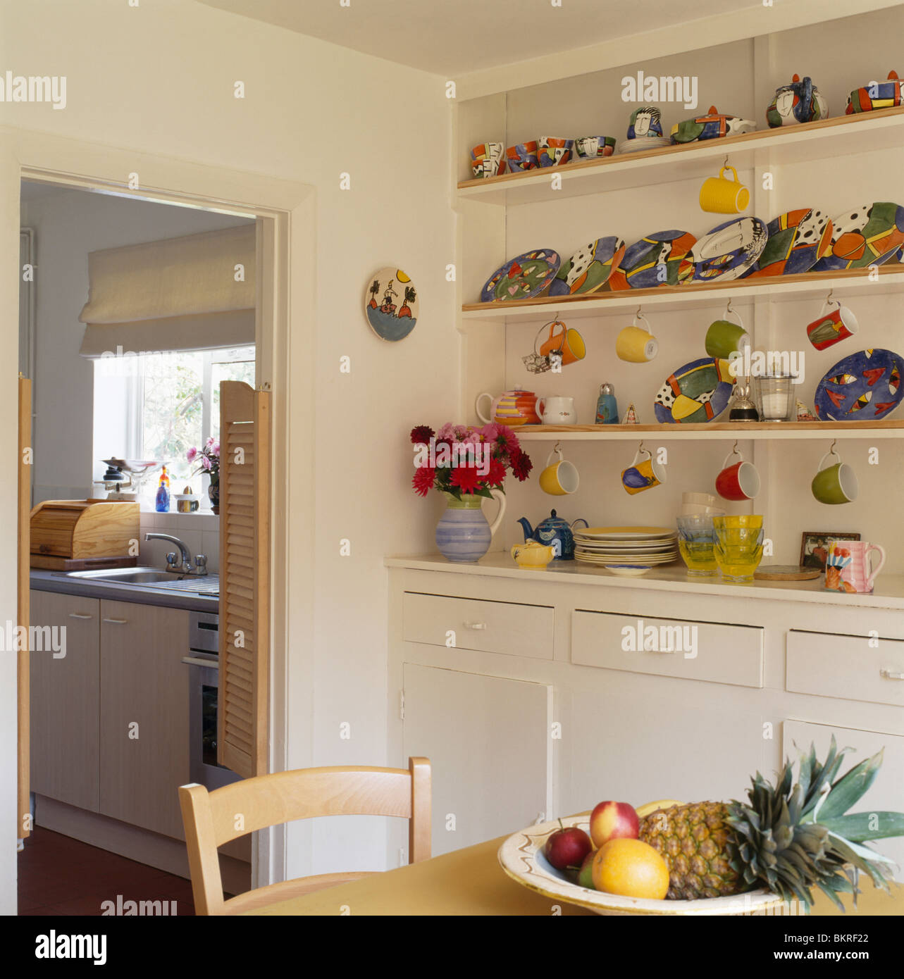 Brightly colored crockery on shelves in dining room with open door to ...