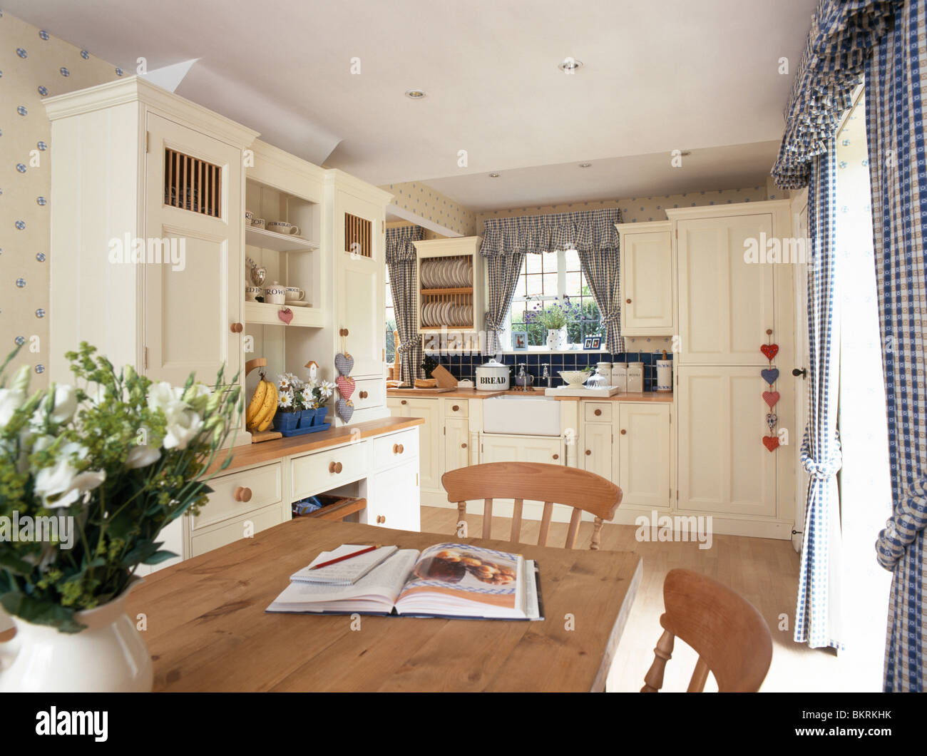 Cream fitted units in country kitchen dining room with wooden table and ...
