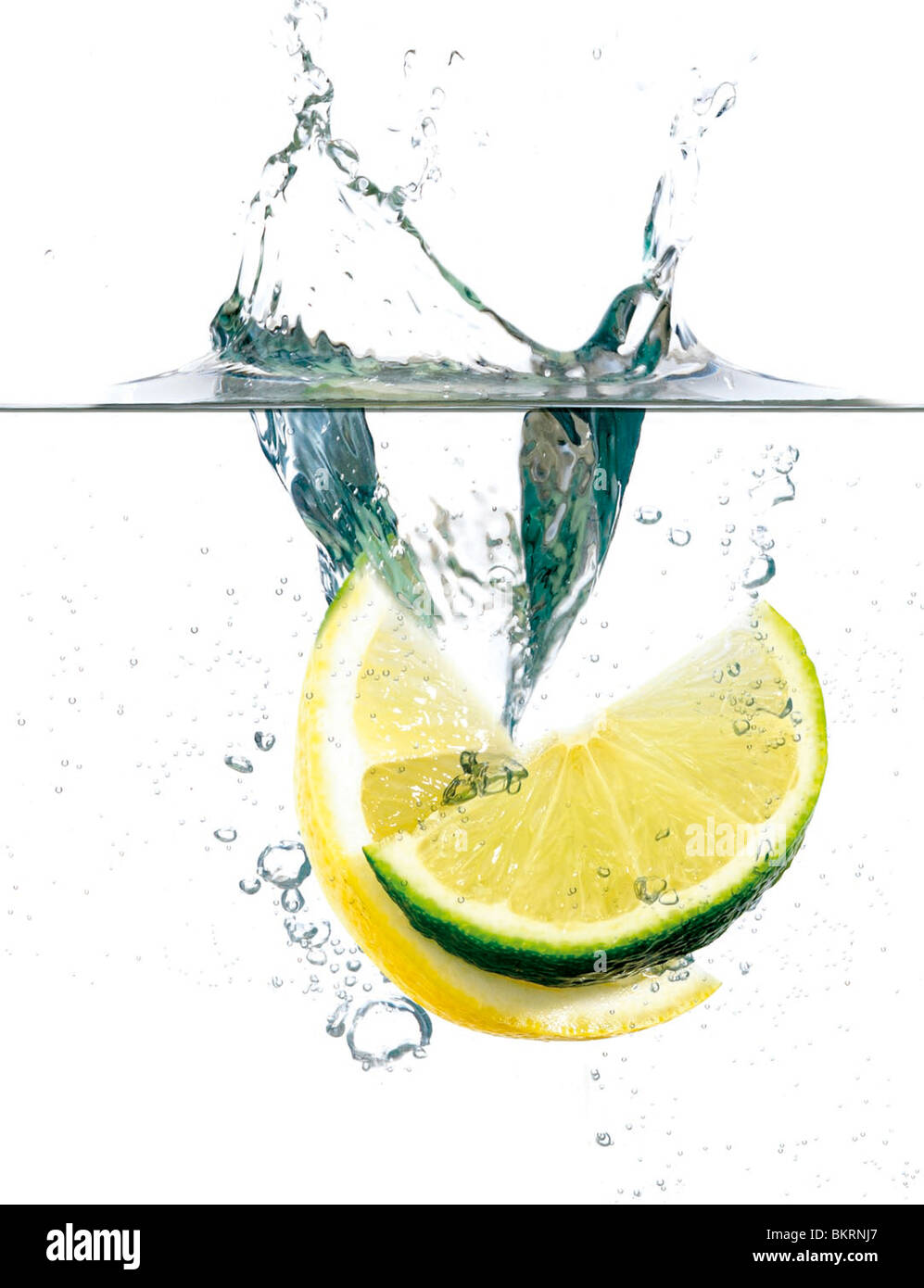 Slices of lemon and lime falling into water, creating a splash, set against white background ...