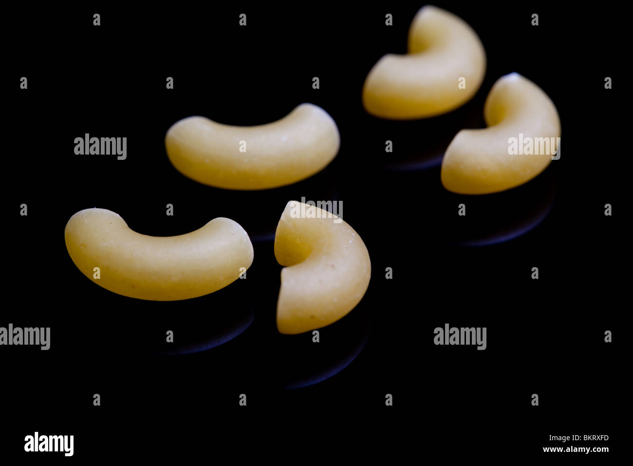 Five pieces of dried macaroni pasta on a black reflective surface Stock ...