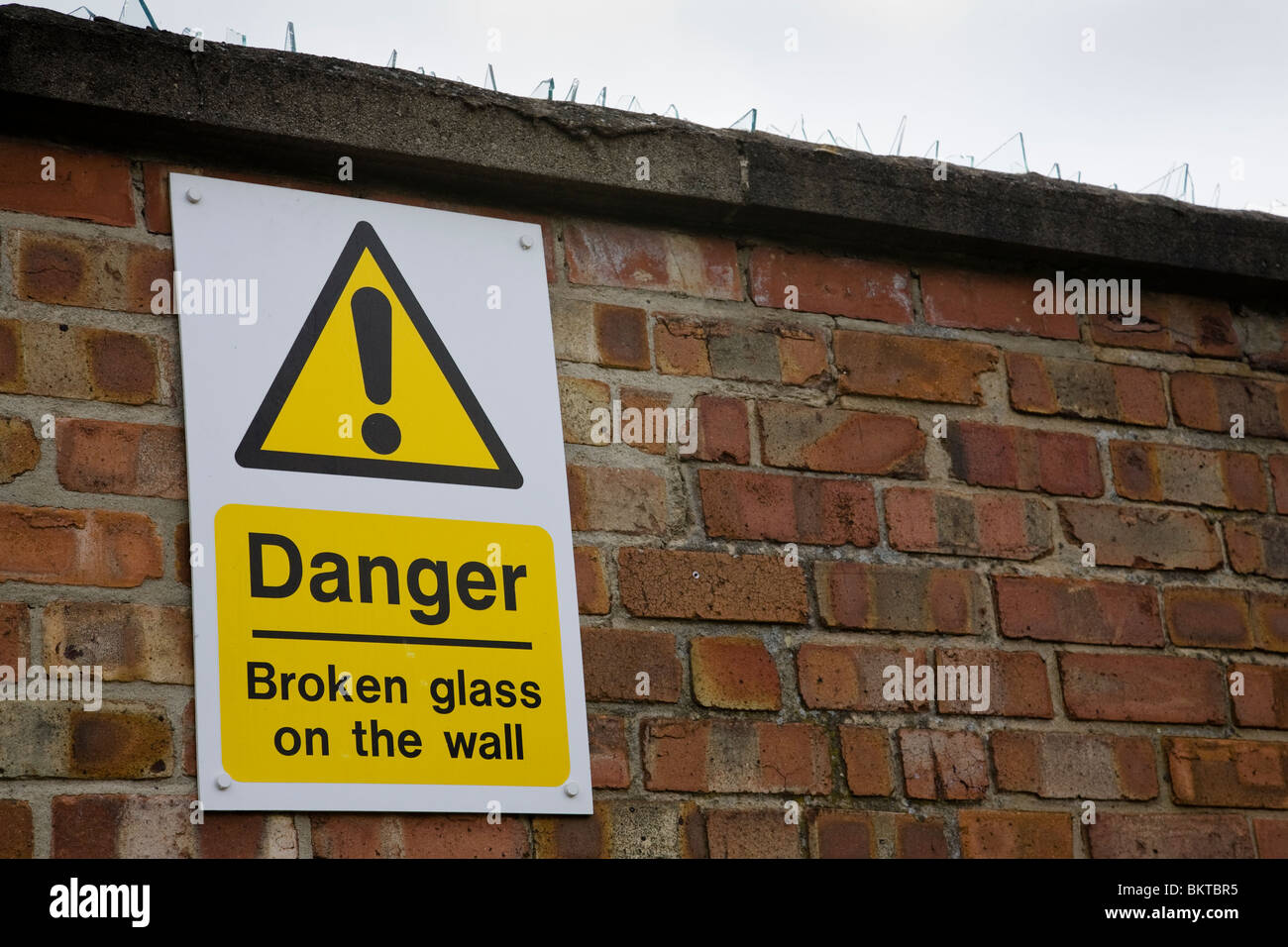 Danger sign warning of broken glass on the top of a wall, England Stock ...