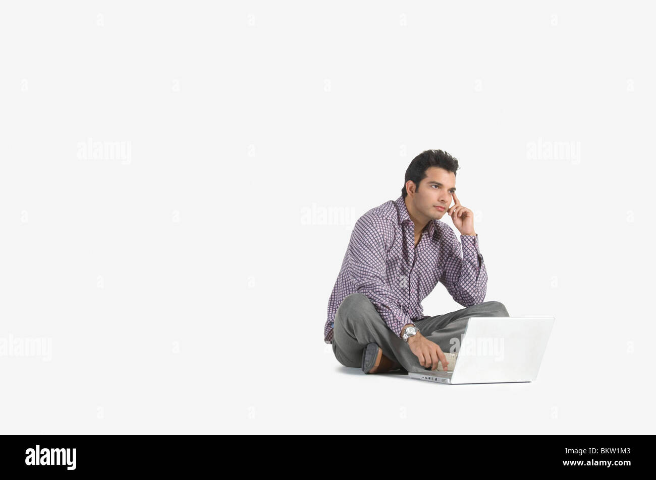Young man sitting with laptop, looking away Stock Photo - Alamy