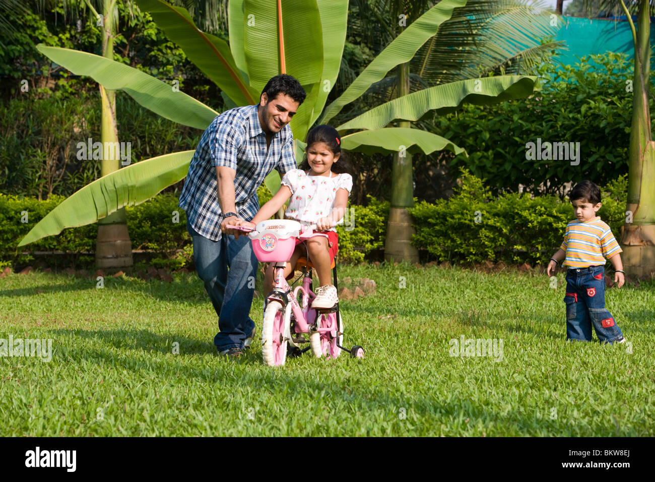 Daughter learning bicycle with her father, son chasing Stock Photo - Alamy
