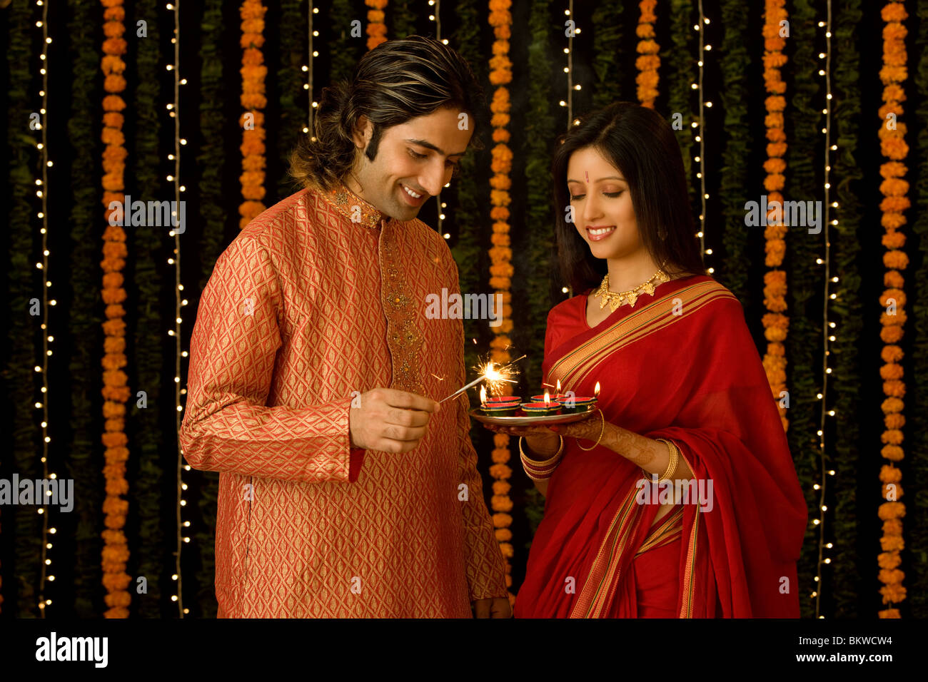 Indian man lighting a small fire work and woman with a plate of candles ...