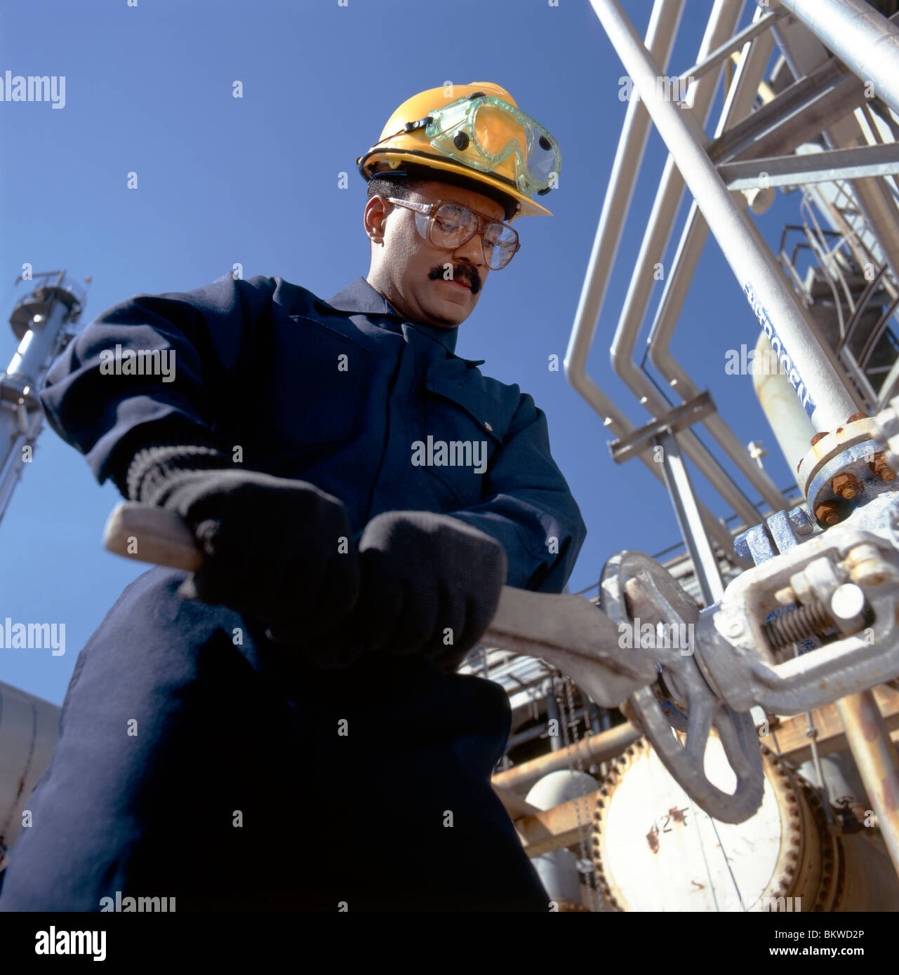 African American worker using a large wrench turns a valve at an oil ...