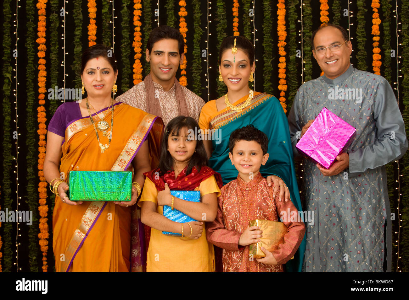 Three generation Indian family holding gift, background flower ...