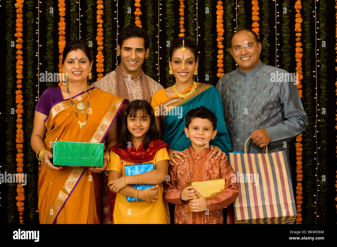 Three generation Indian family holding gift, background flower ...