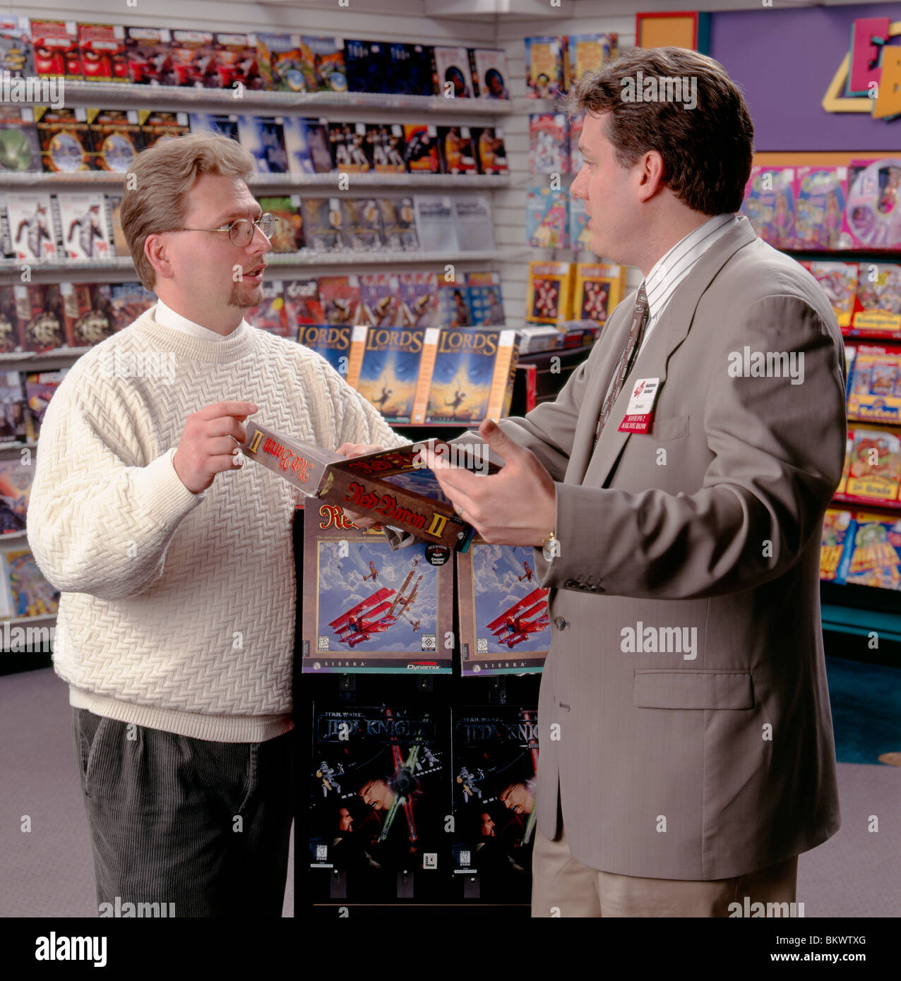 Adult male sales clerk showing a male customer a gaming software ...