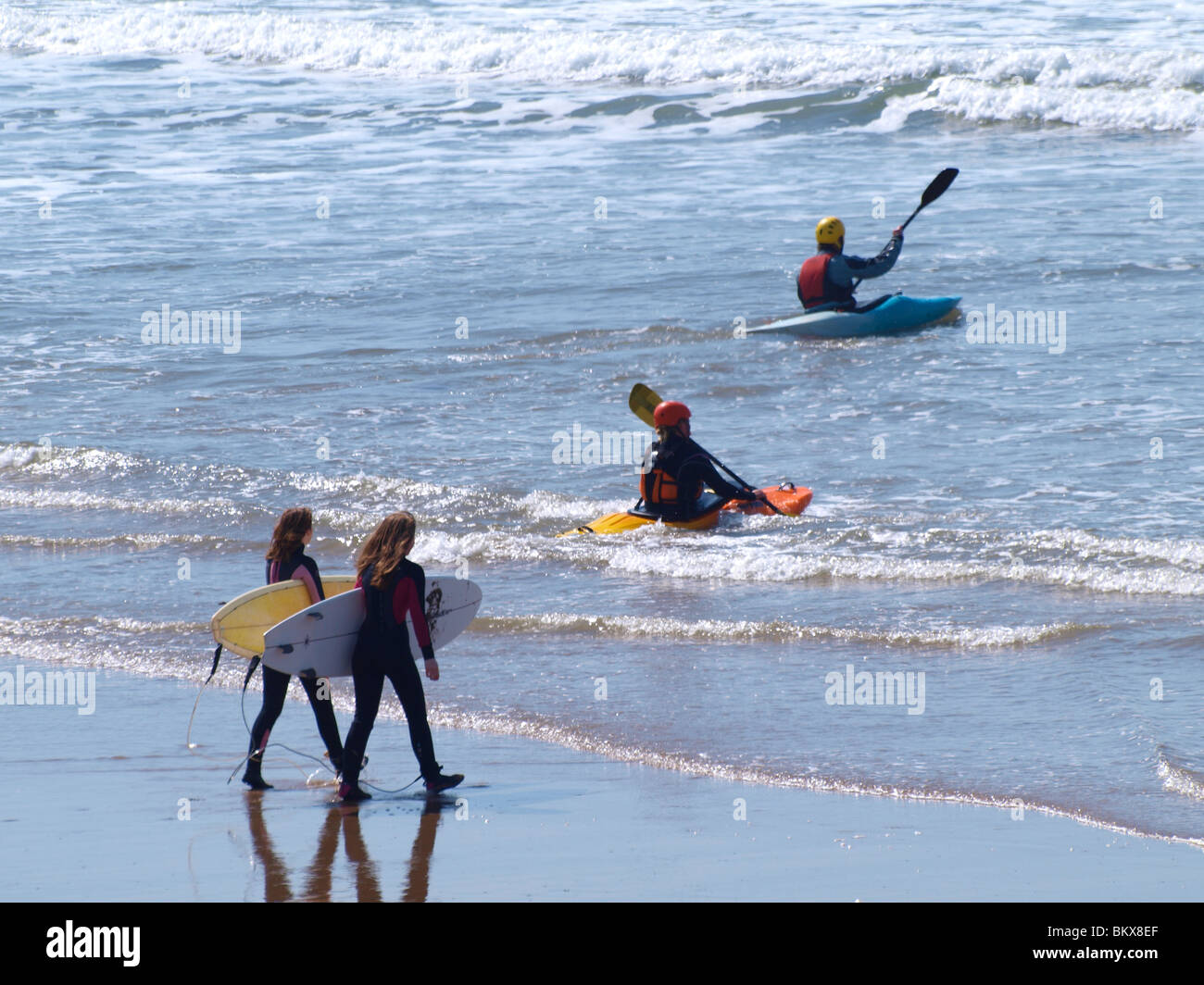 Two surf kayakers paddling out and to female surfers heading for the ...