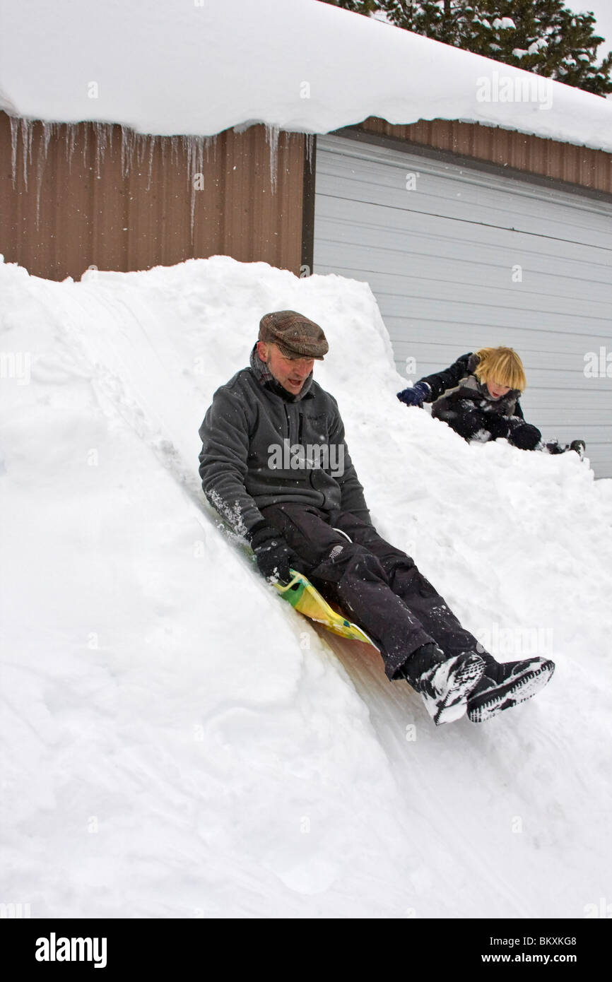 Man plays with sled, sliding down gentle, short slope at the side of a ...