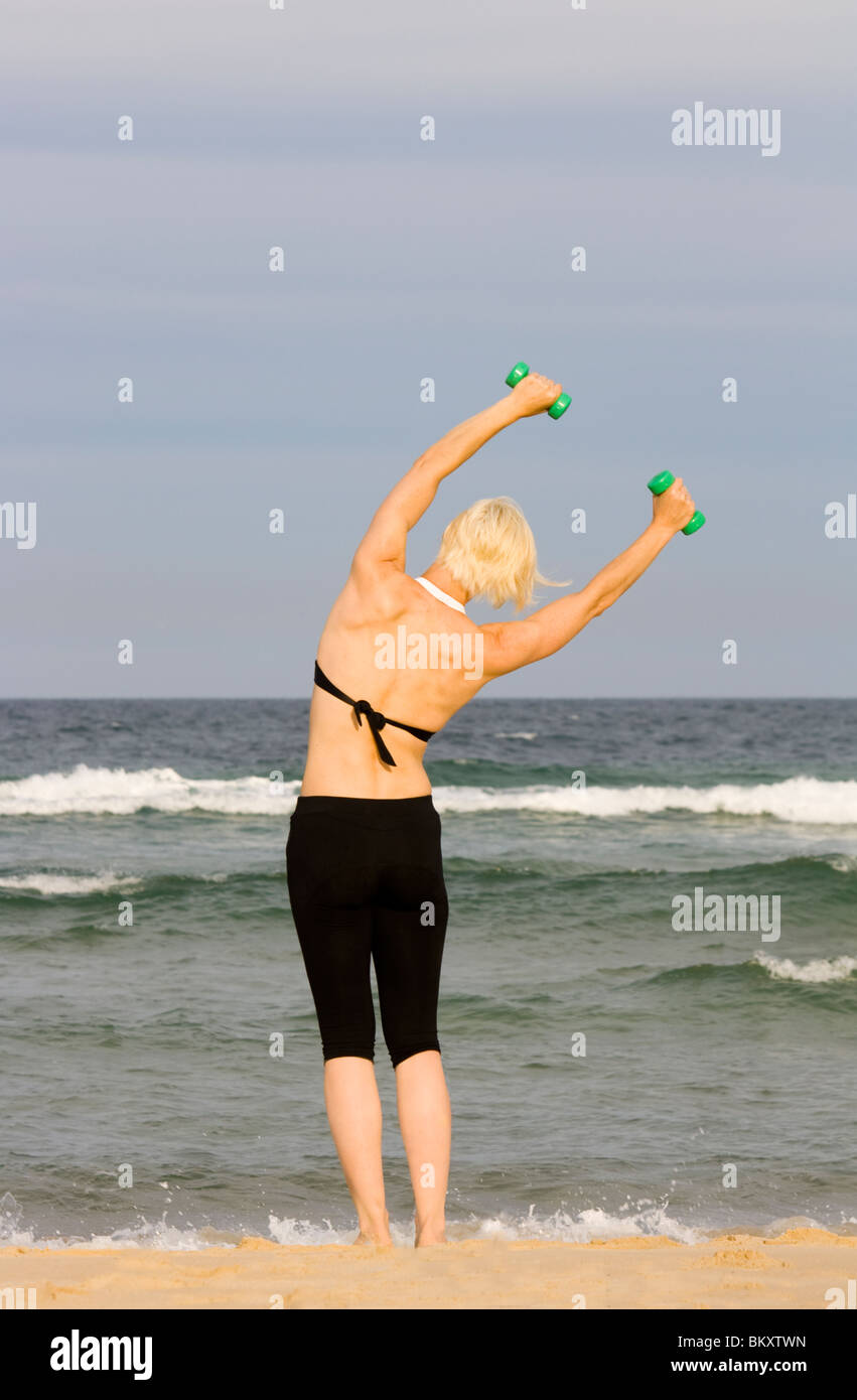 healthy woman stretching on the beach with dumbells. Beach fitness ...