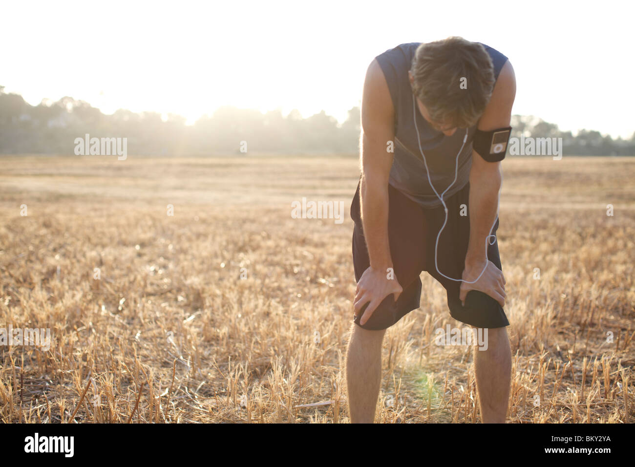 Male runner in his late 20's catches his breath as he finishes his run ...