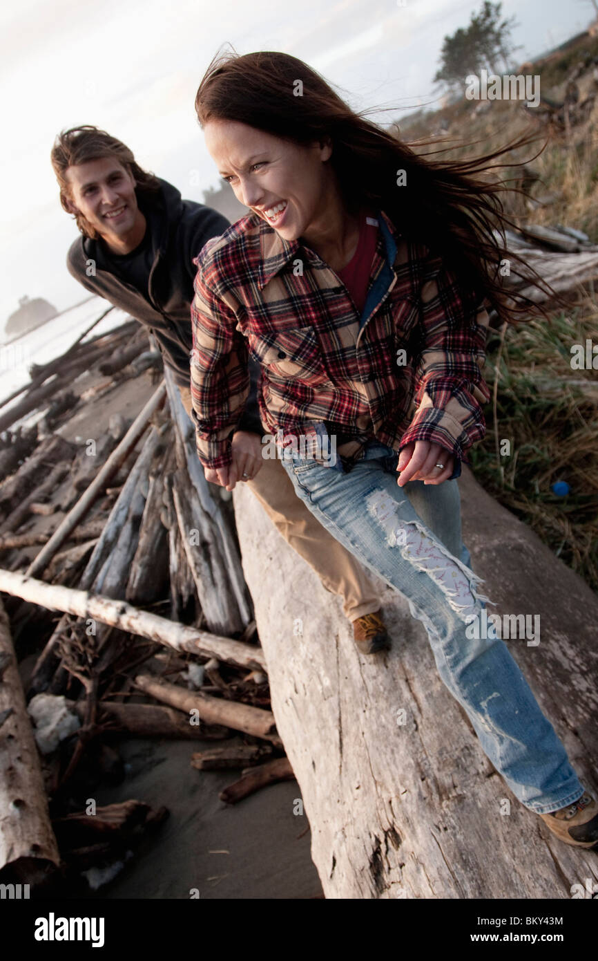 A young couple smile while walking along a beach log Stock Photo - Alamy