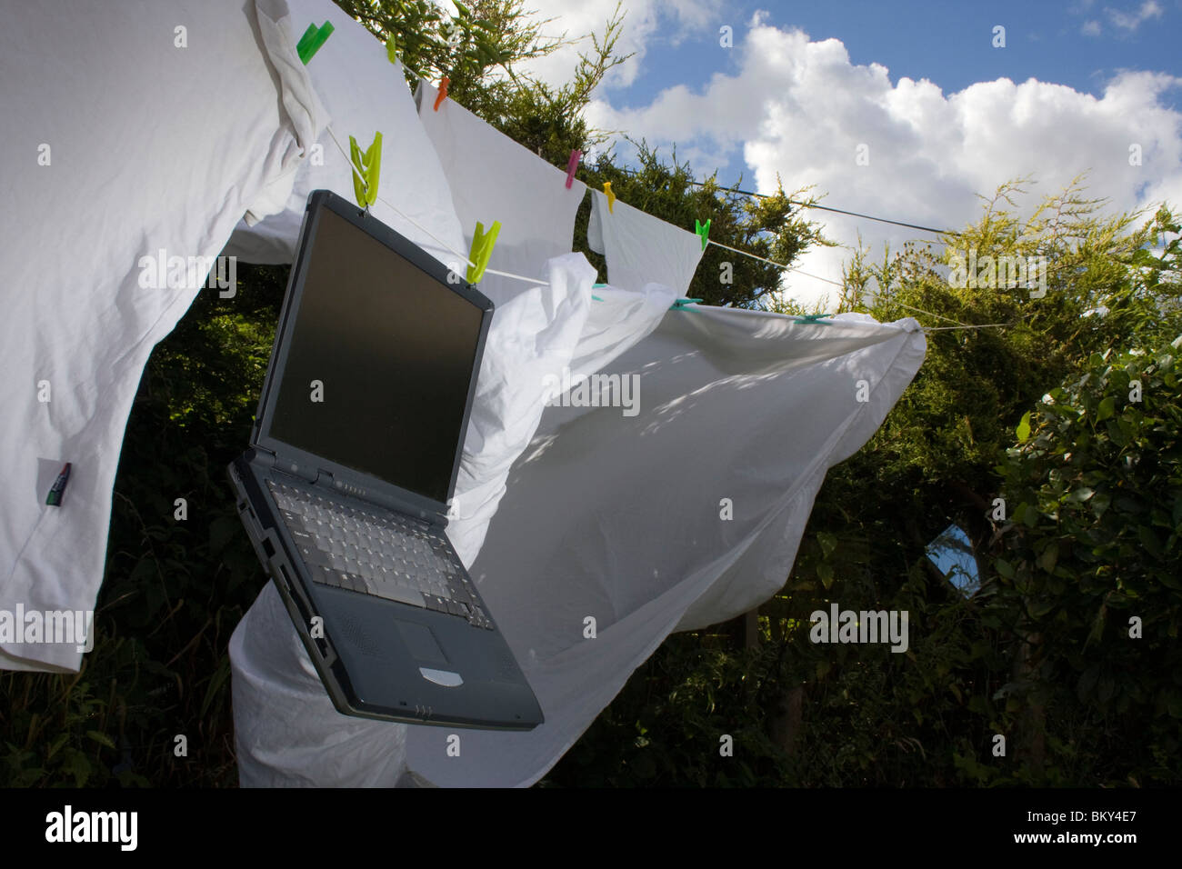 A gray laptop computer hangs on a washing line with white sheets ...