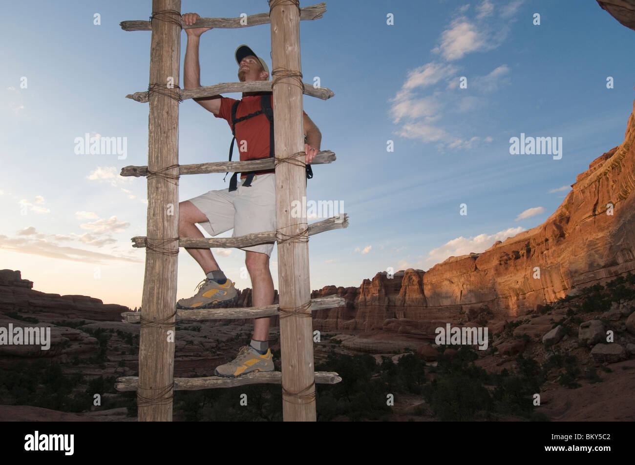 A man climbing a wooden ladder while hiking along a sandstone trail ...