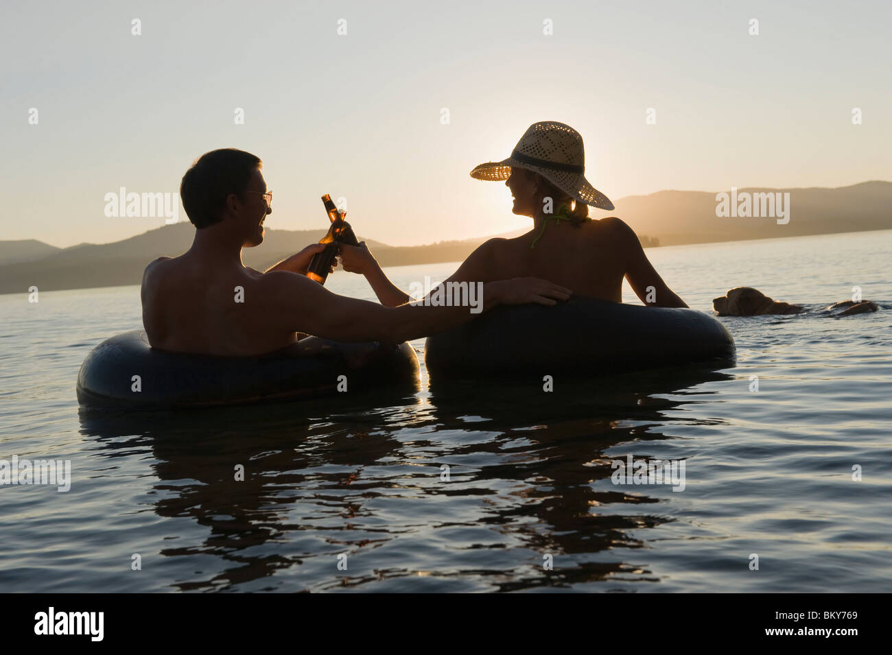 A young couple relax with a cold beverage while floating in a lake at ...