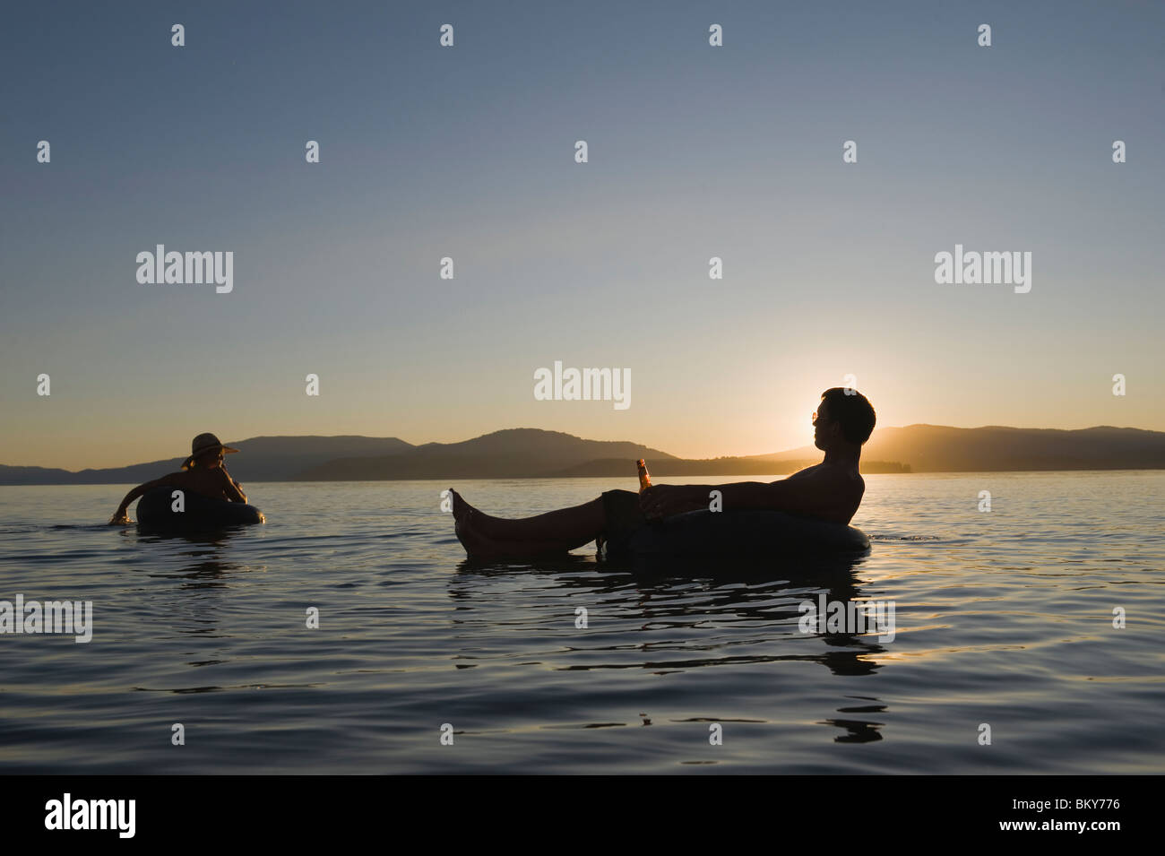 A young couple relax with a cold beverage while floating in a lake at ...