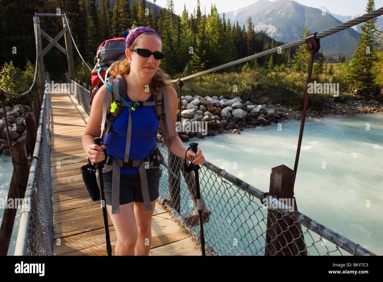 A female backpacker in her early thirties crosses a suspension bridge ...