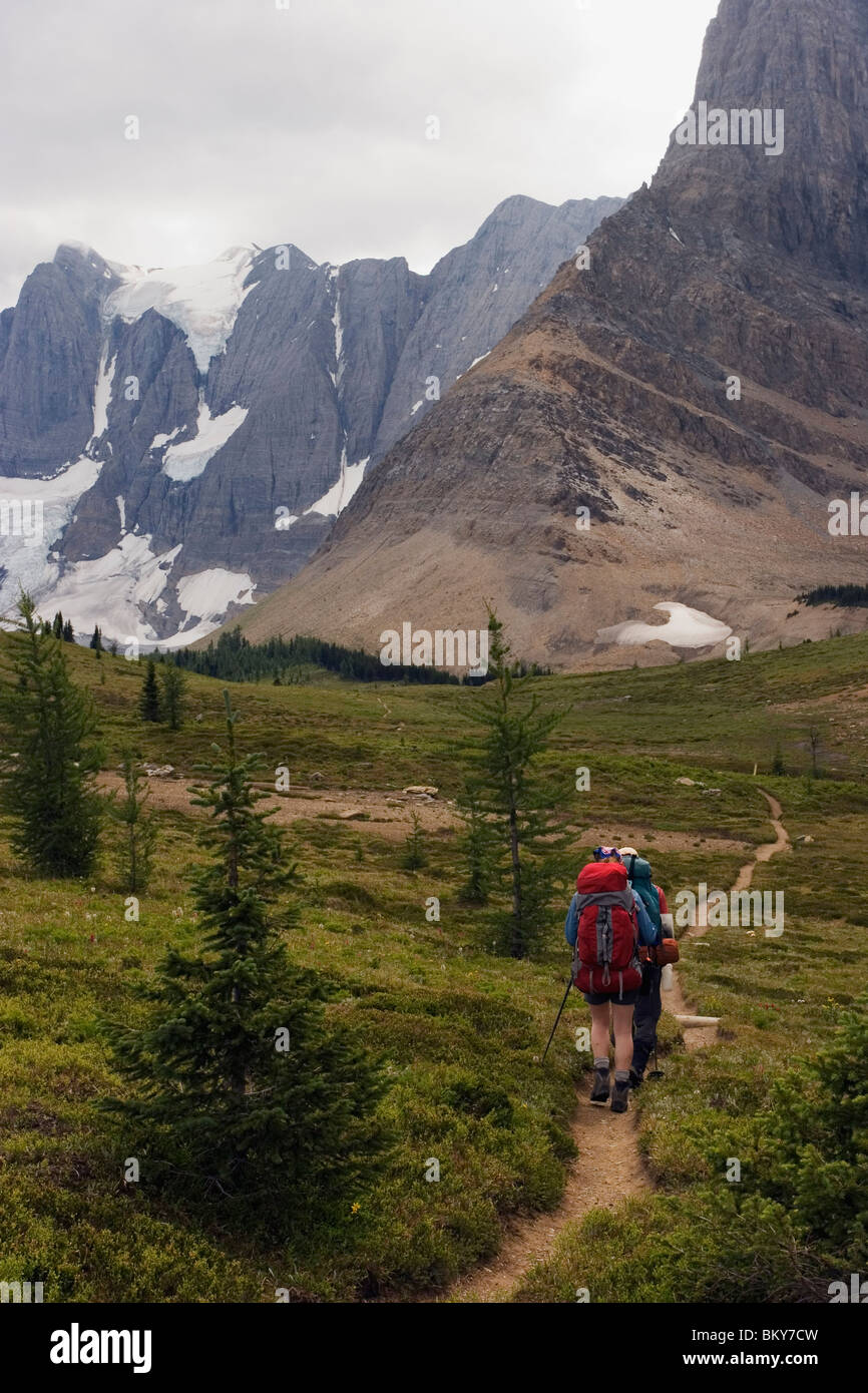 Two backpackers hike towards the towering limestone cliffs and glaciers ...