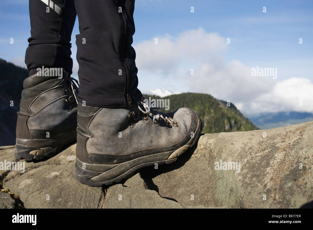 A low shot of a backpacker's lower legs and boots, standing on granite ...