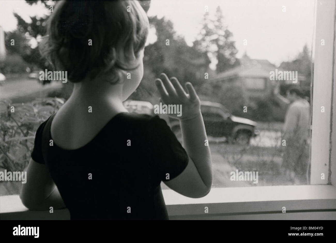 Rear view of girl looking through window and waving Stock Photo - Alamy