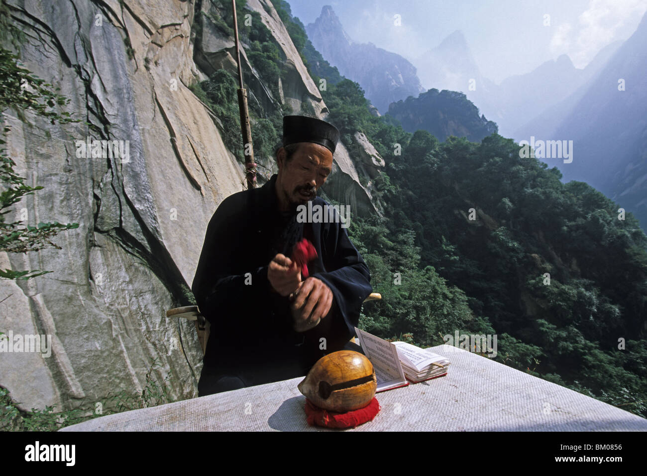 Taoist hermit monk prays in front of his hut, cliff, Hua Shan, Shaanxi ...