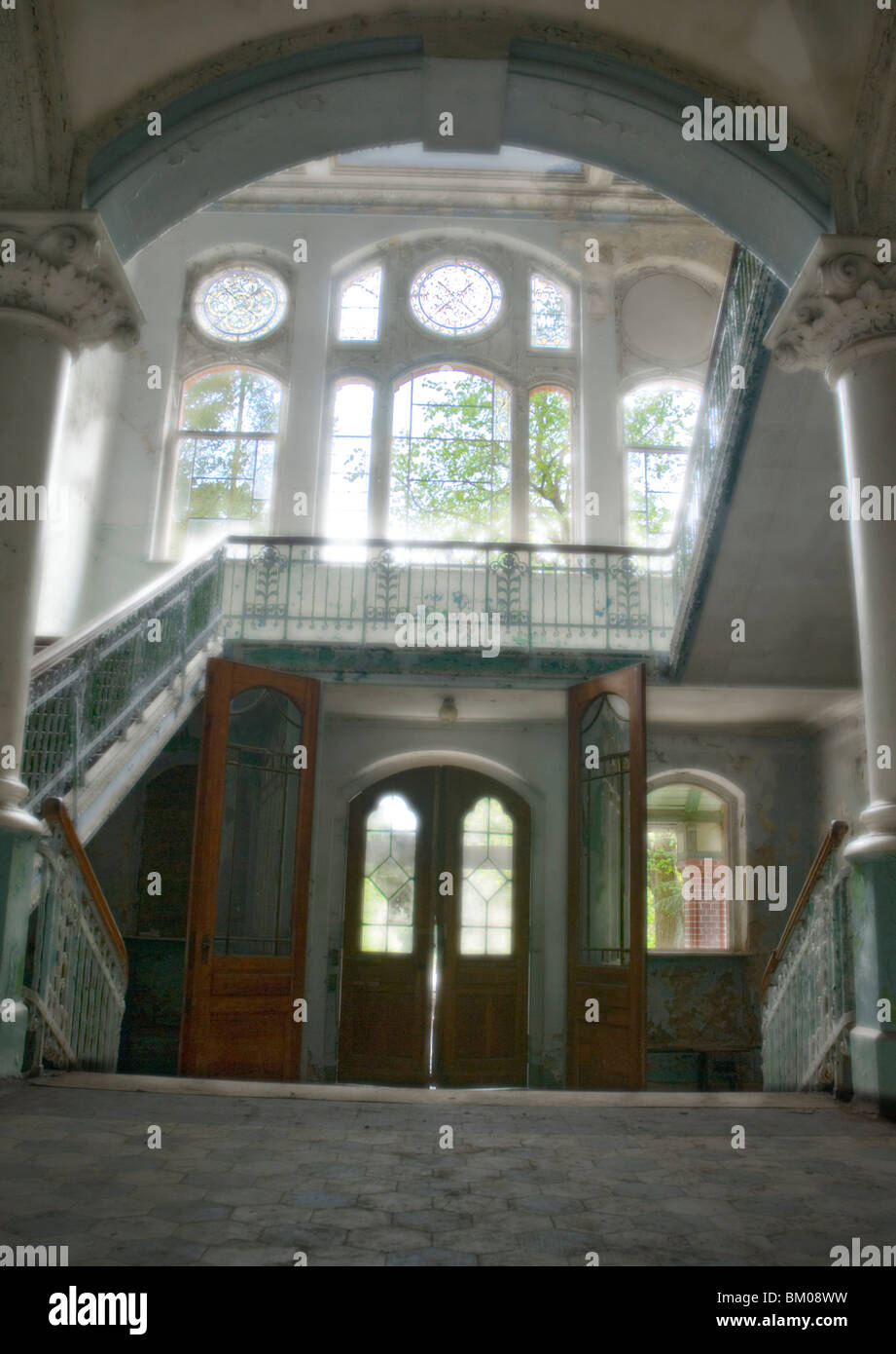 Grand entrance with large windows and staircase in old disused hospital ...
