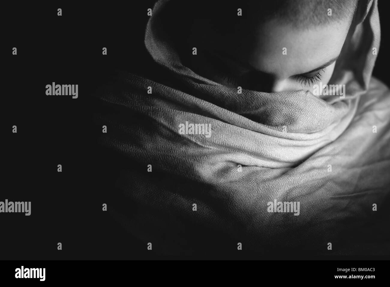 A woman looks down with the lower half of her face covered by a scarf ...