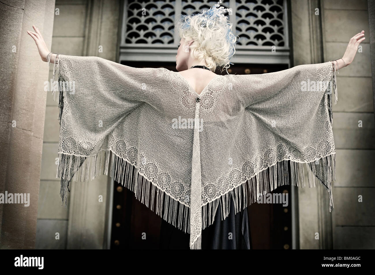 The back of a woman with blonde and blue hair wearing a shawl spreads ...