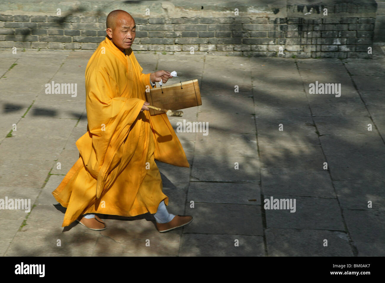 monk in yellow rope calls with a wooden drum for the prayer, during ...