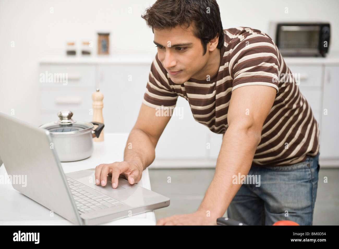 Man using a laptop on a kitchen counter Stock Photo - Alamy