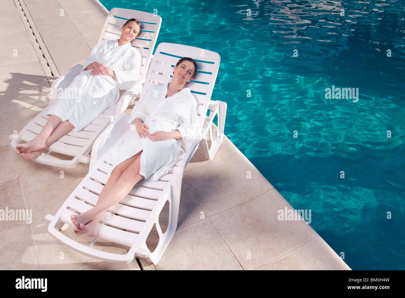 Two women resting on lounge chairs at poolside Stock Photo - Alamy