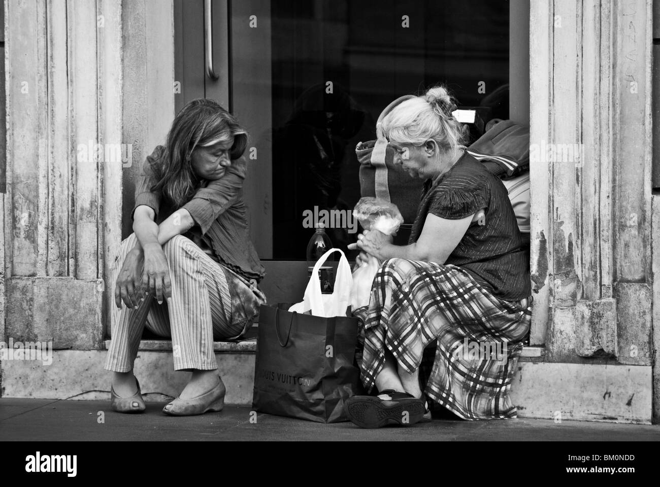 Two homeless old women sitting by the pavement in front of a building ...